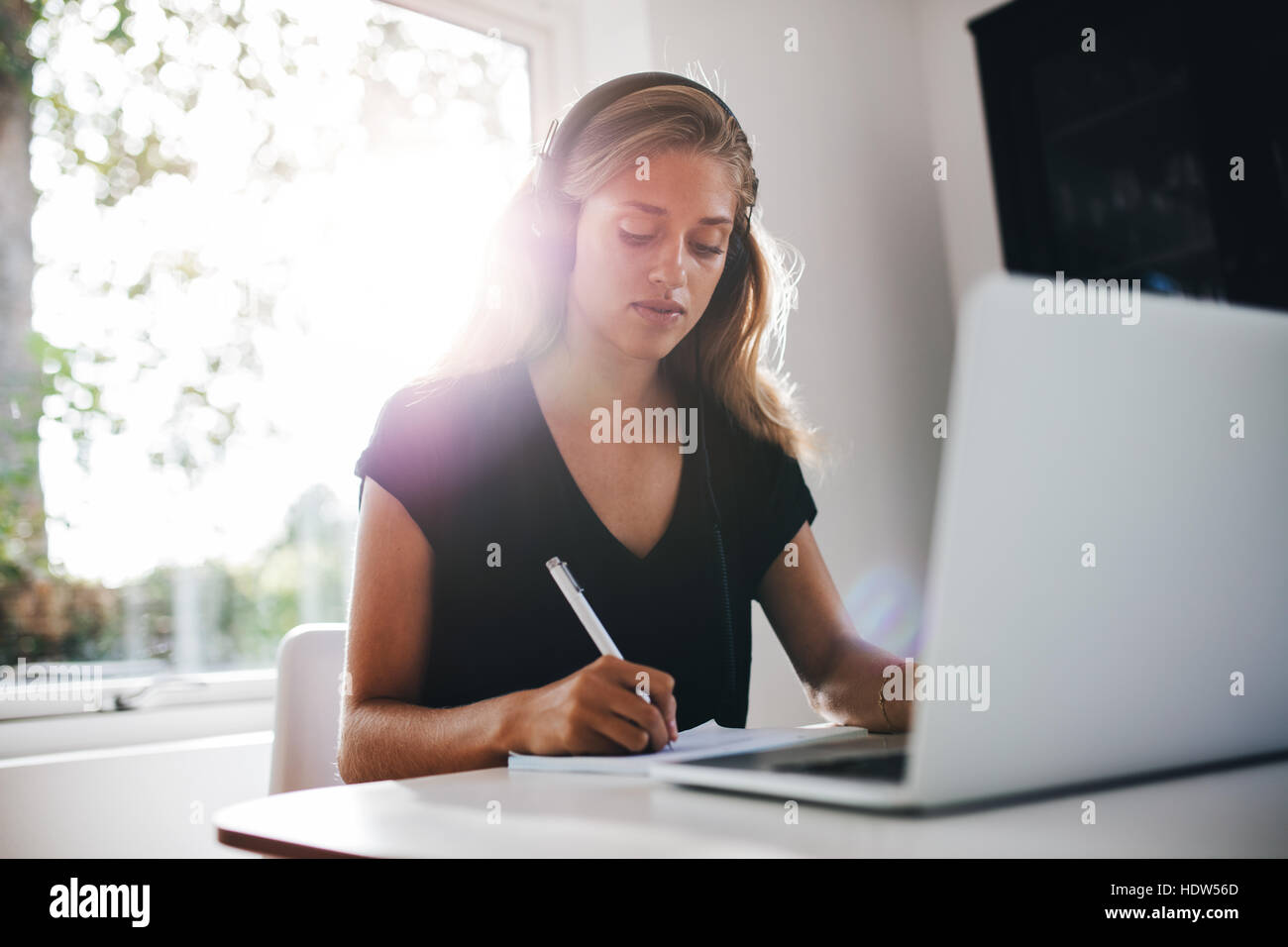 Indoor shot of young woman studying on kitchen. Female writing on book ...