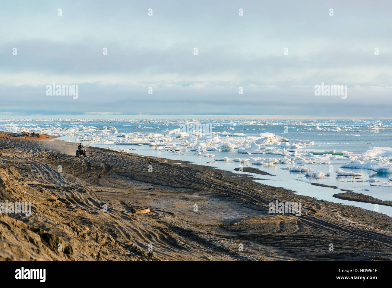 Two native Alaskan men drive an ATV down a sand beach along the Arctic ...