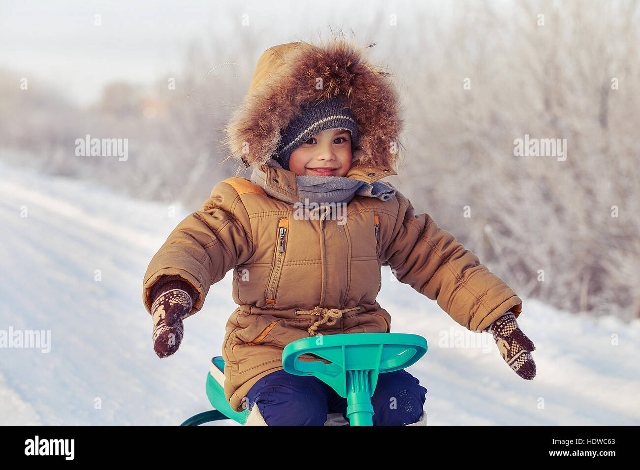 Little boy riding his kids snowmobile winter snow-covered road in the ...