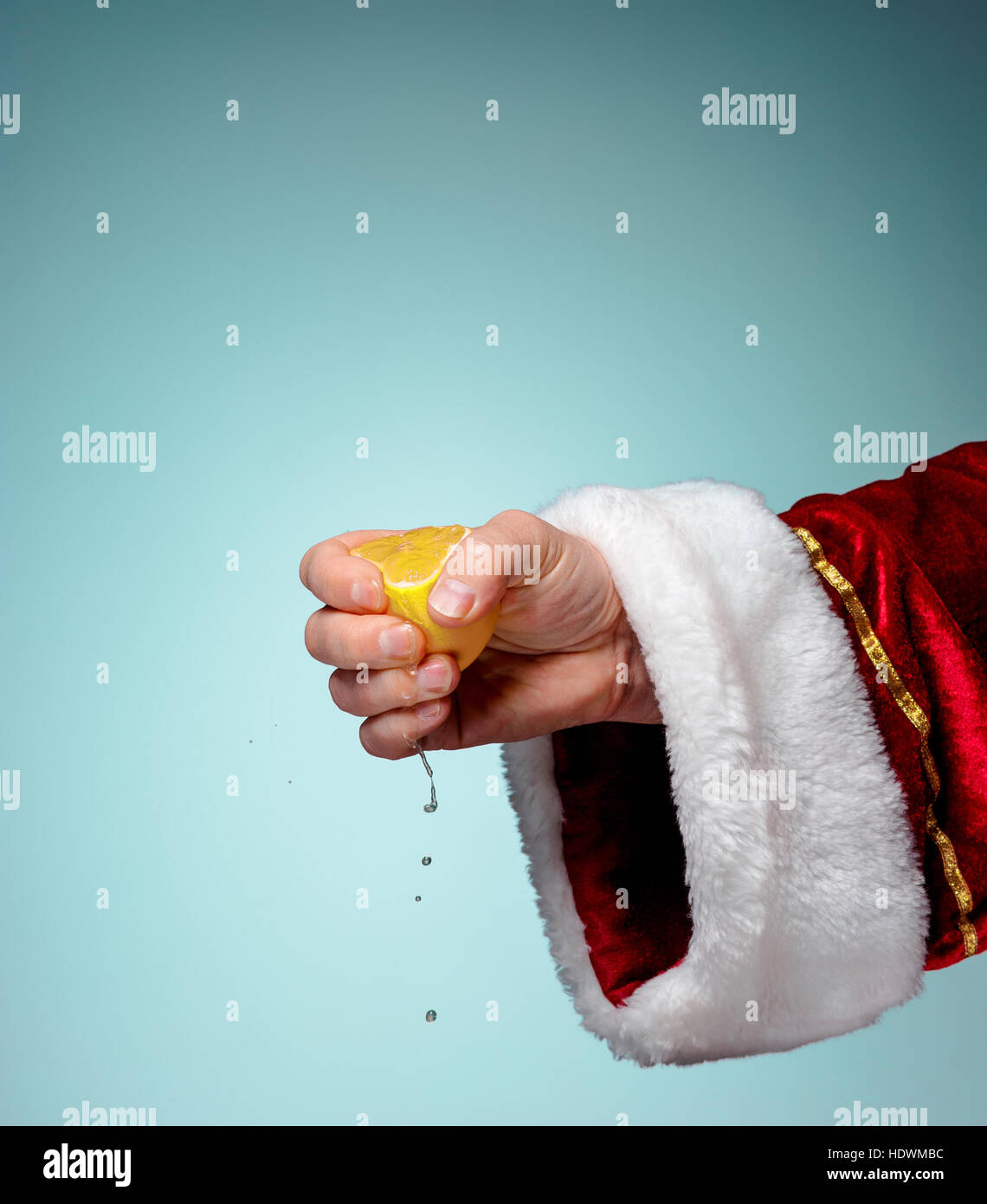 Photo of Santa Claus Hand squeezing lemon on blue Stock Photo - Alamy