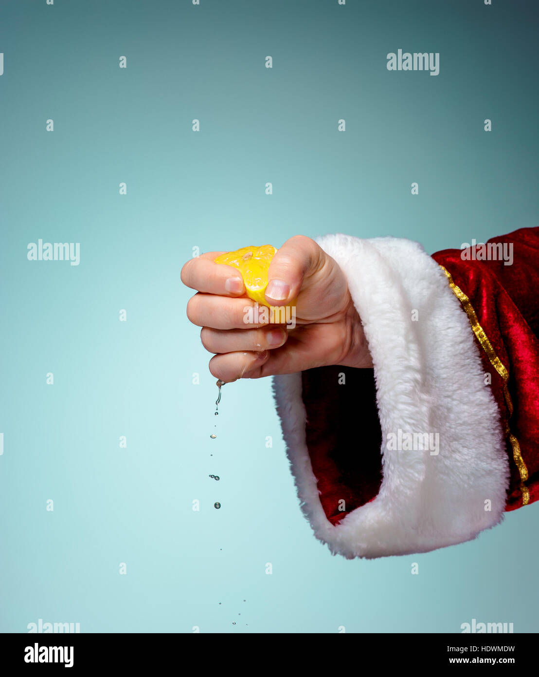 Photo of Santa Claus Hand squeezing lemon on blue Stock Photo - Alamy