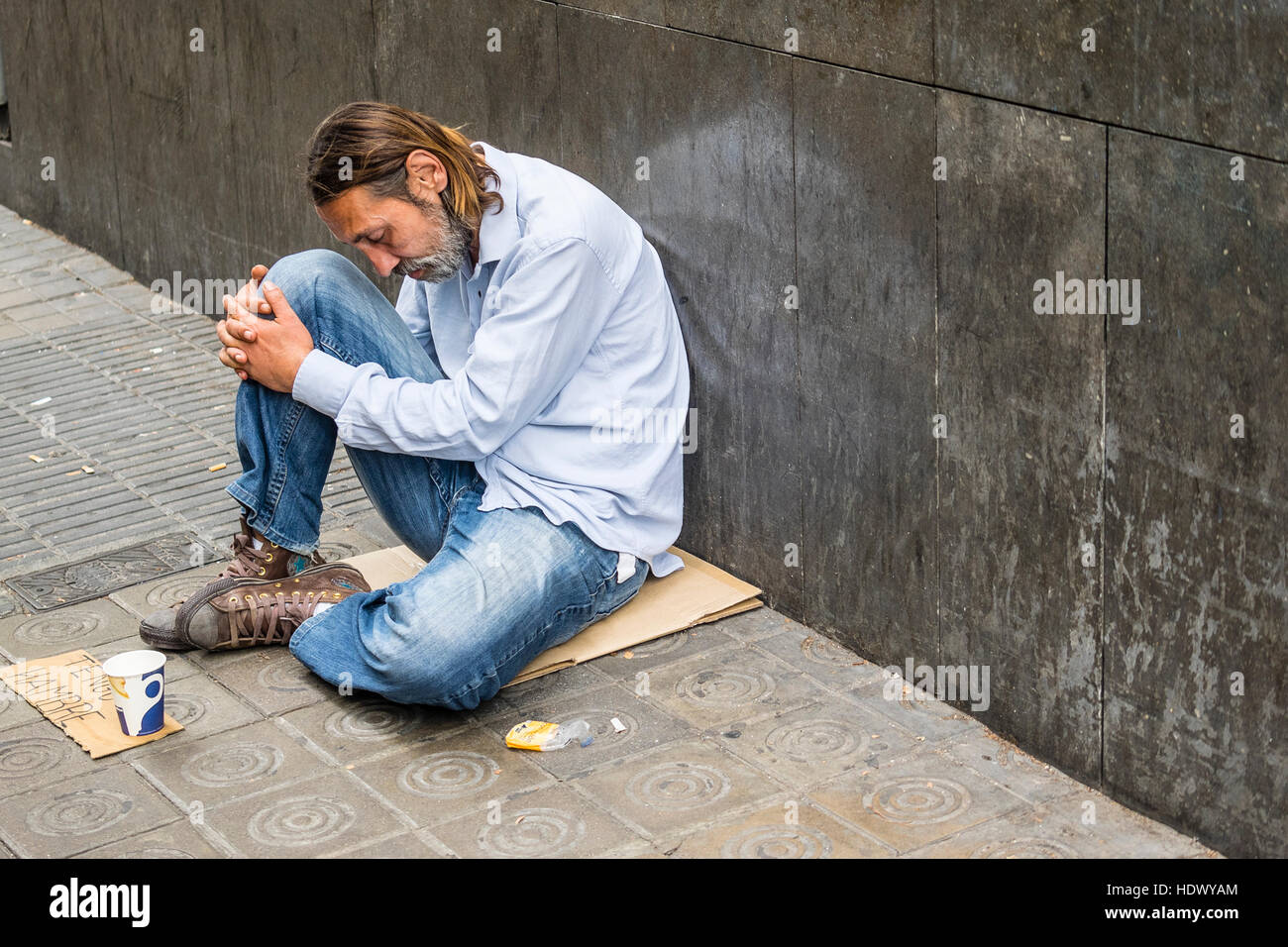 Male Beggar sits on a piece of cardboard and has a sign on cardboard ...