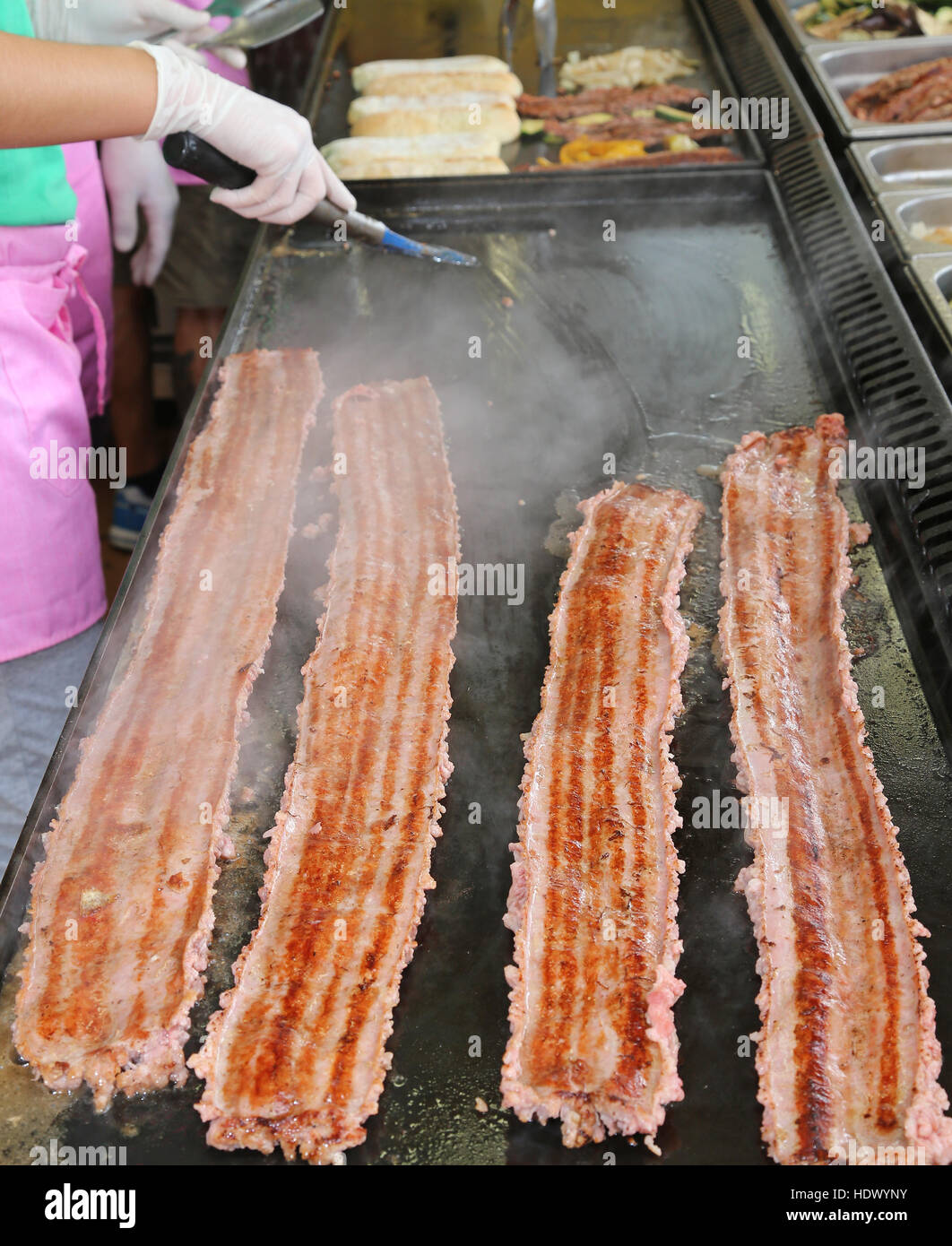 long strip of meat cooked on the hot plate in the stand of street foods ...