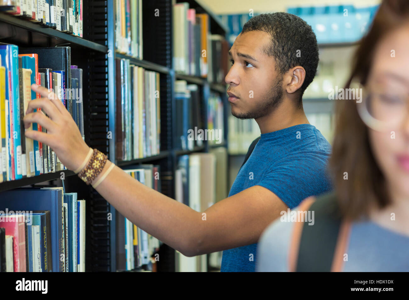 Mixed Race boy choosing book in library Stock Photo - Alamy