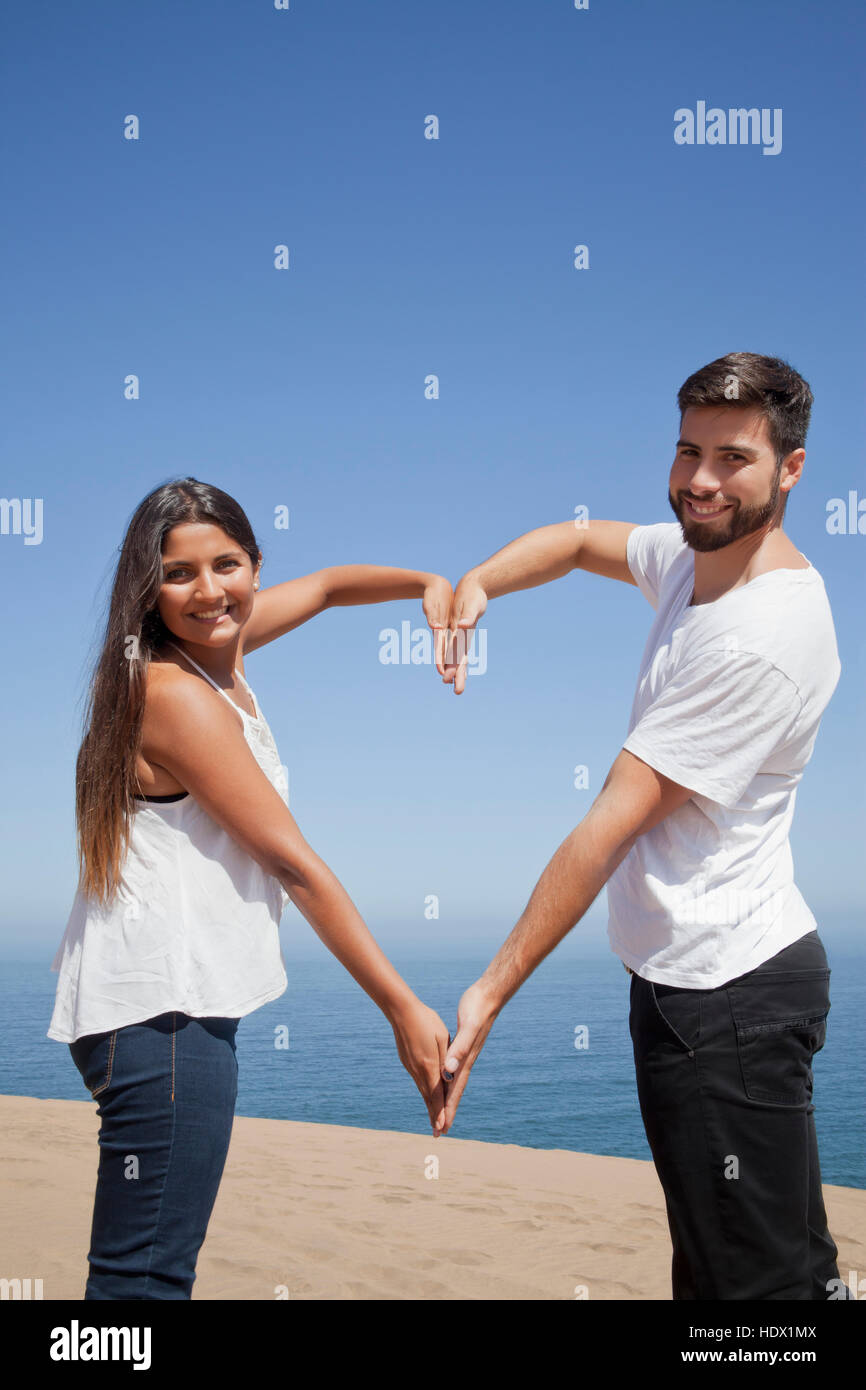 Hispanic couple making heart-shape with arms at beach Stock Photo - Alamy