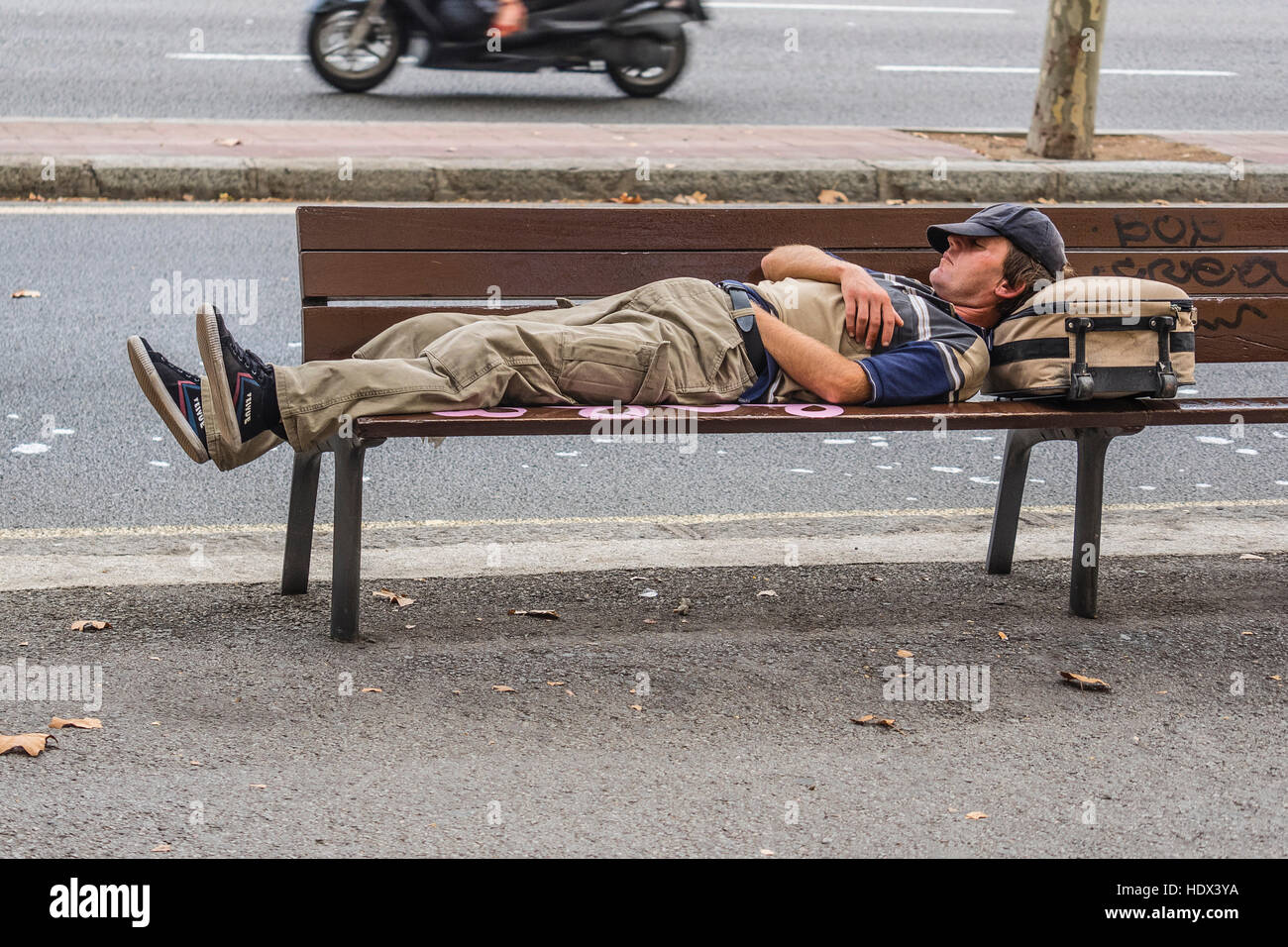 Male napping on a city bench in Barcelona, Spain with his hat over his ...