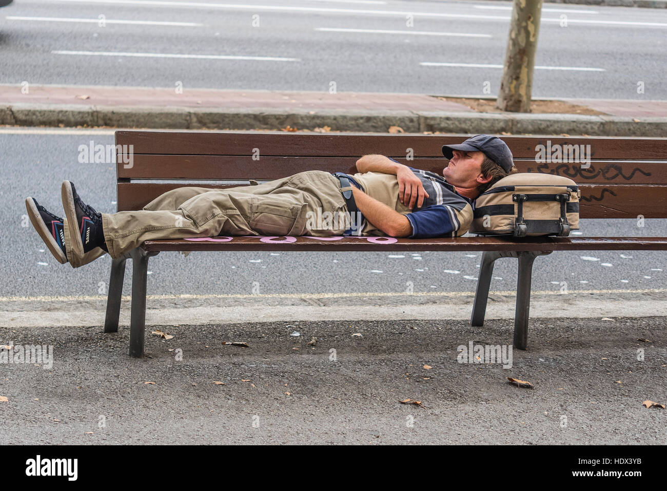 Male napping on a city bench in Barcelona, Spain with his hat over his ...