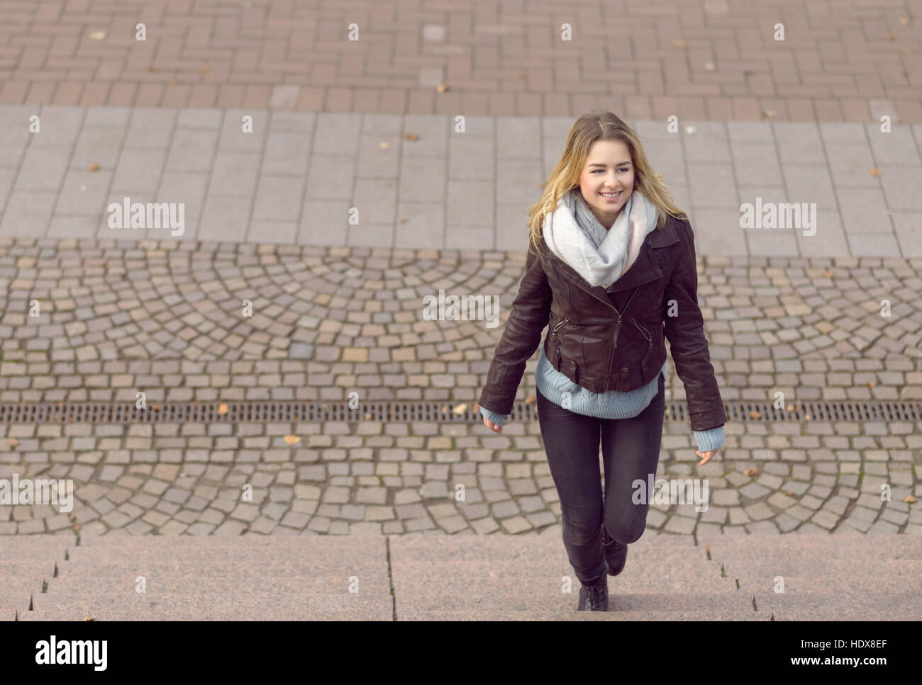 Smiling trendy young woman walking up steps outdoors with copyspace ...