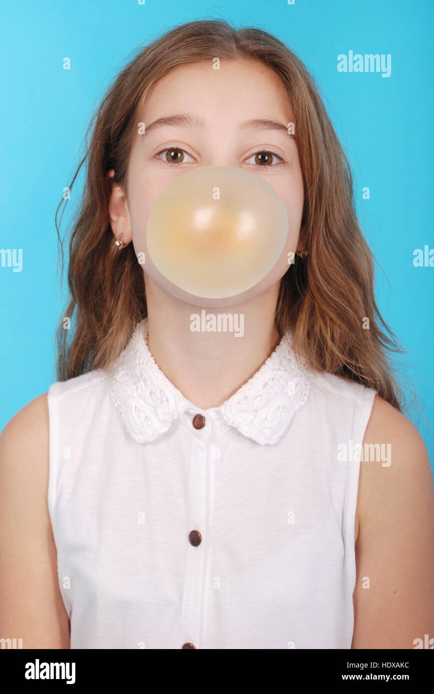 Young girl making a big bubble with a chewing gum isolated on blue ...