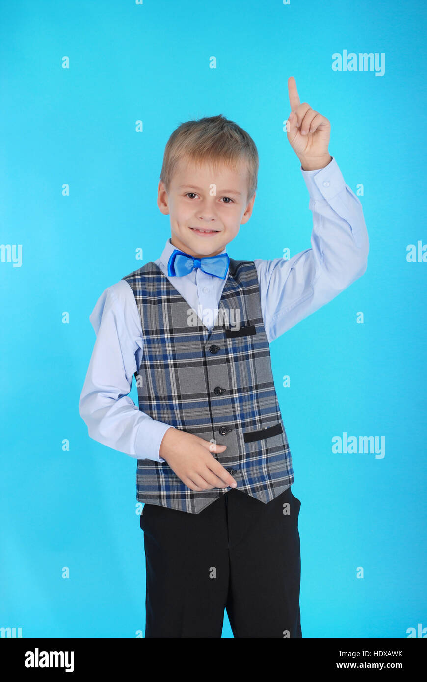 Boy in school uniform holding a raised index finger on the blue ...