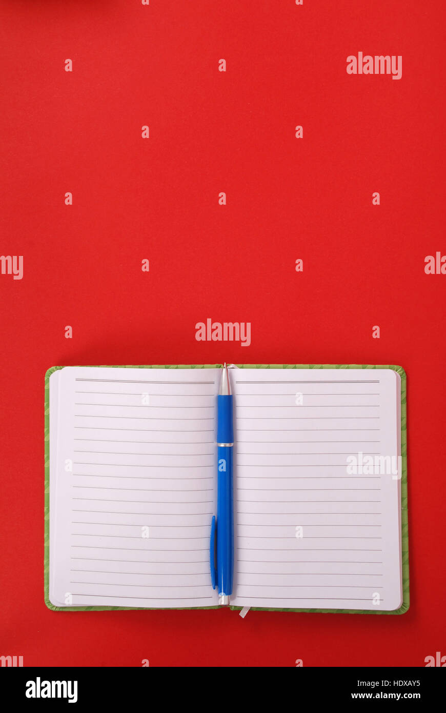 Green notebook with blue pen isolated on red background with soft ...