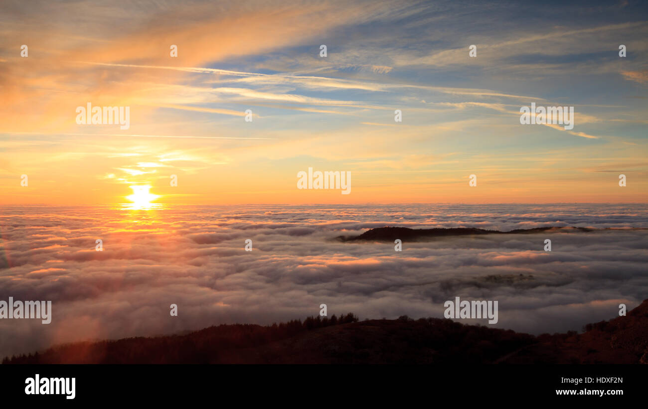 Landscape with the sun setting behind clouds and fog Stock Photo - Alamy
