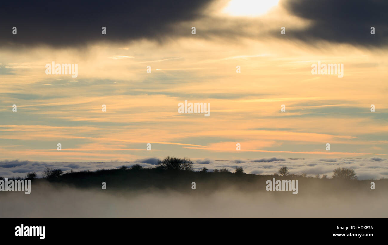 Landscape with the sun setting behind clouds and fog Stock Photo - Alamy