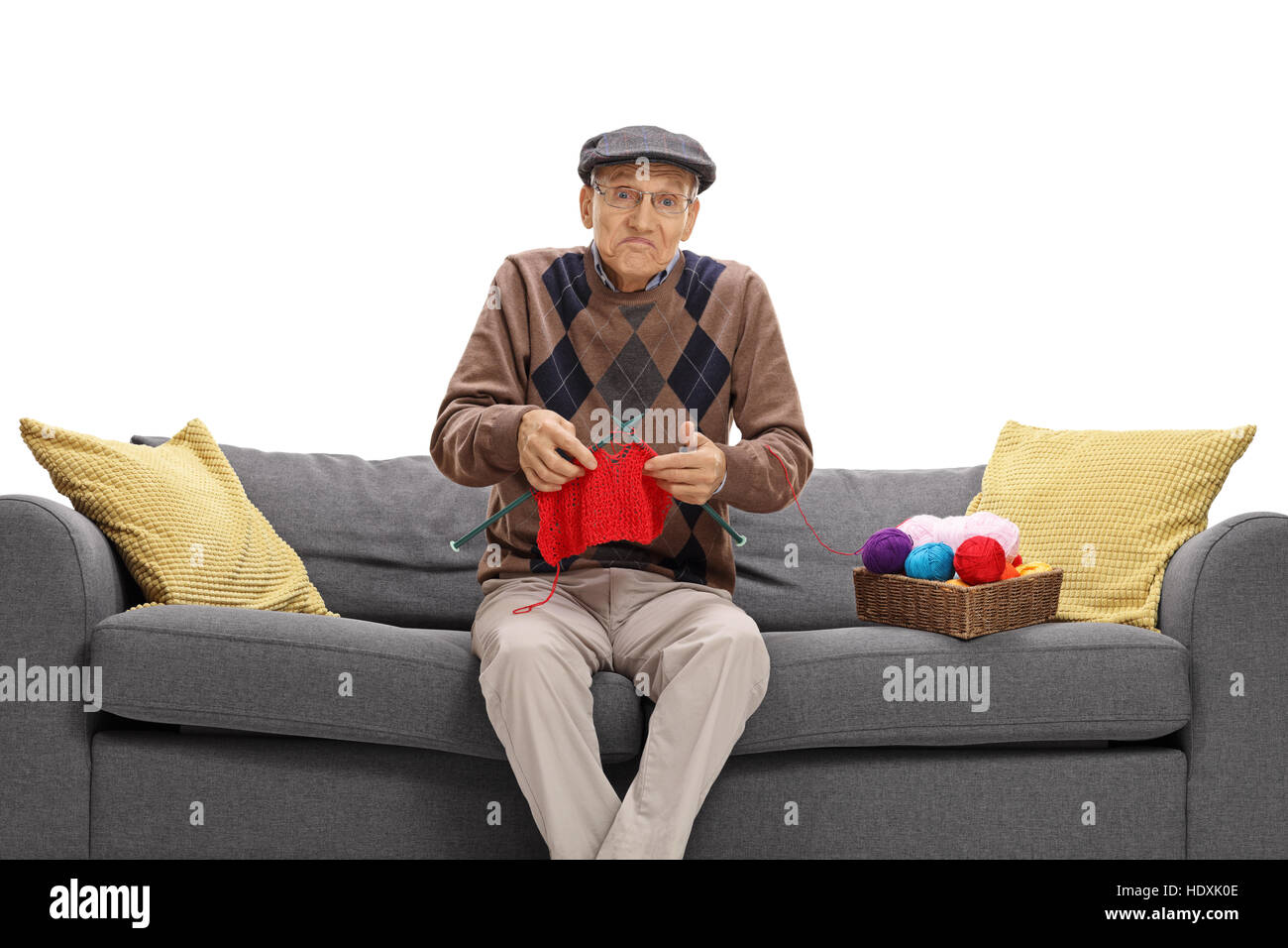 Confused elderly man sitting on a sofa and knitting isolated on white ...