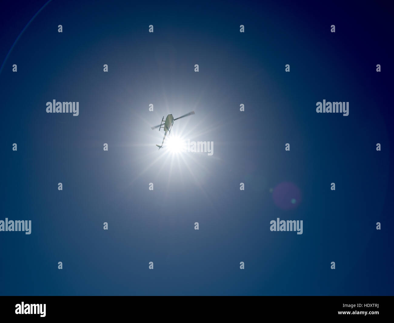 Looking up at the sun, in a clear blue sky, as a tour helicopter flies ...