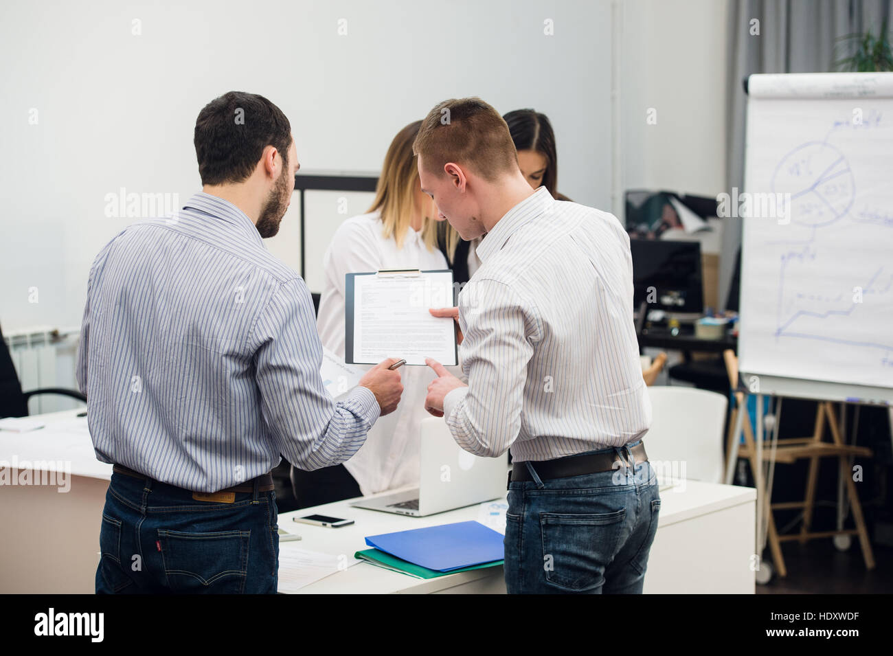 Four young business people working as a team gathered around laptop ...