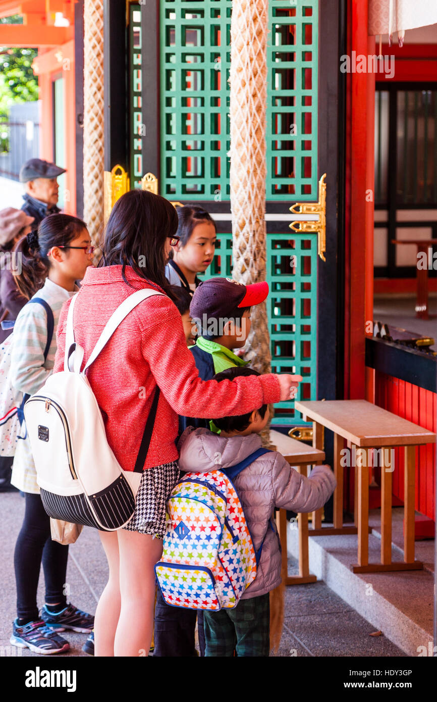 Japan, Kobe, Ikuta Shinto Shrine. Woman and three children shaking bell ...