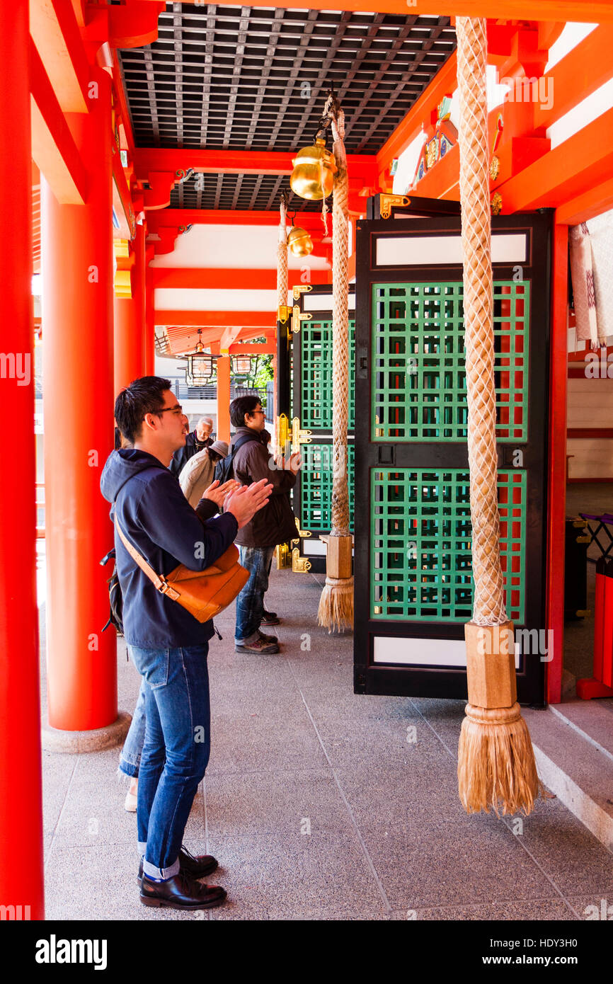 Japan, Kobe, Ikuta Shinto Shrine. Man and woman clapping while praying ...