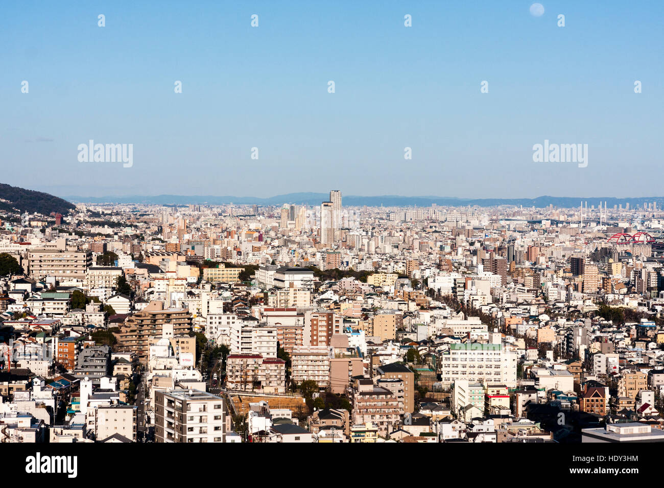 Japan, Kobe. Daytime moon in clear blue sky, seen over Kobe city. High viewpoint, cityscape ...