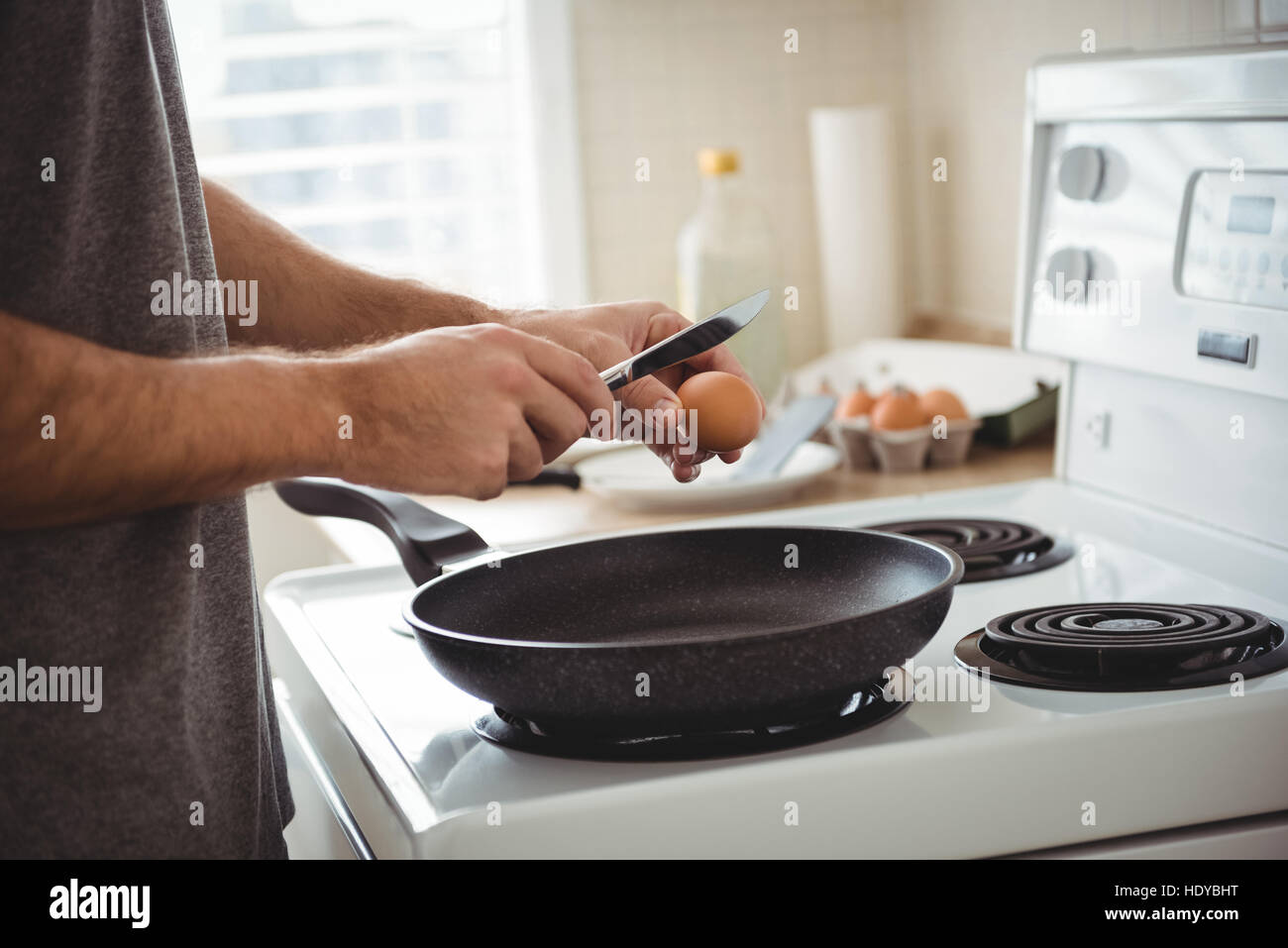Mid section of man cracking an egg into a frying pan in the kitchen at ...