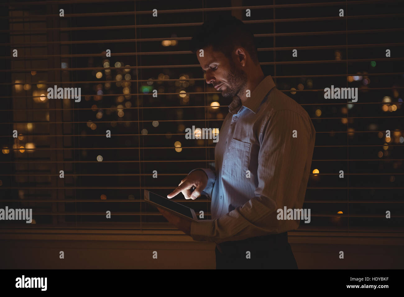 Man using his digital tablet near window blinds at night Stock Photo ...