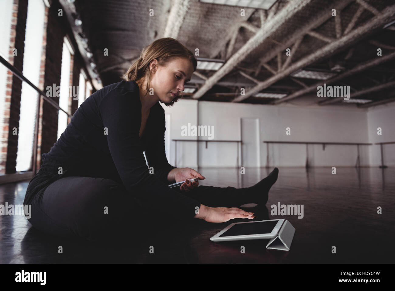 Dancer sitting on floor and using digital tablet in dance studio Stock ...