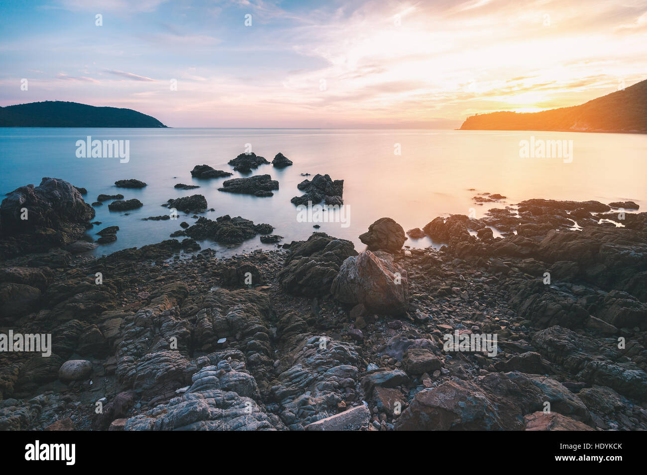 Black rock beach with smooth milky sea surface and sunset behind ...