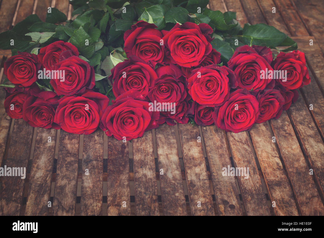 dark red roses laying on wooden table, retro toned Stock Photo - Alamy