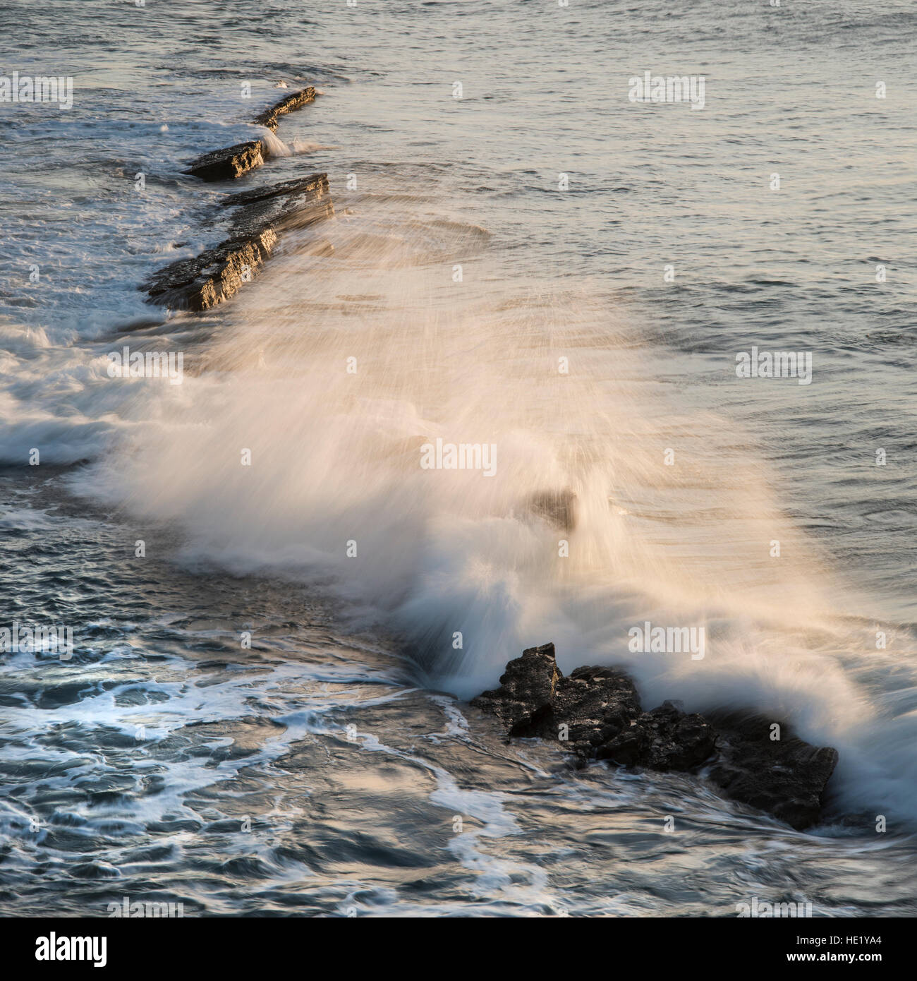 Wave crashing over rocks in ocean at sunrise Stock Photo - Alamy