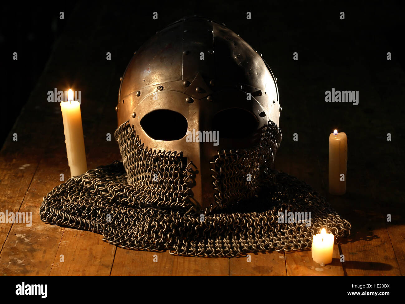 Ancient knight helmet with hauberk near candles on wooden background ...