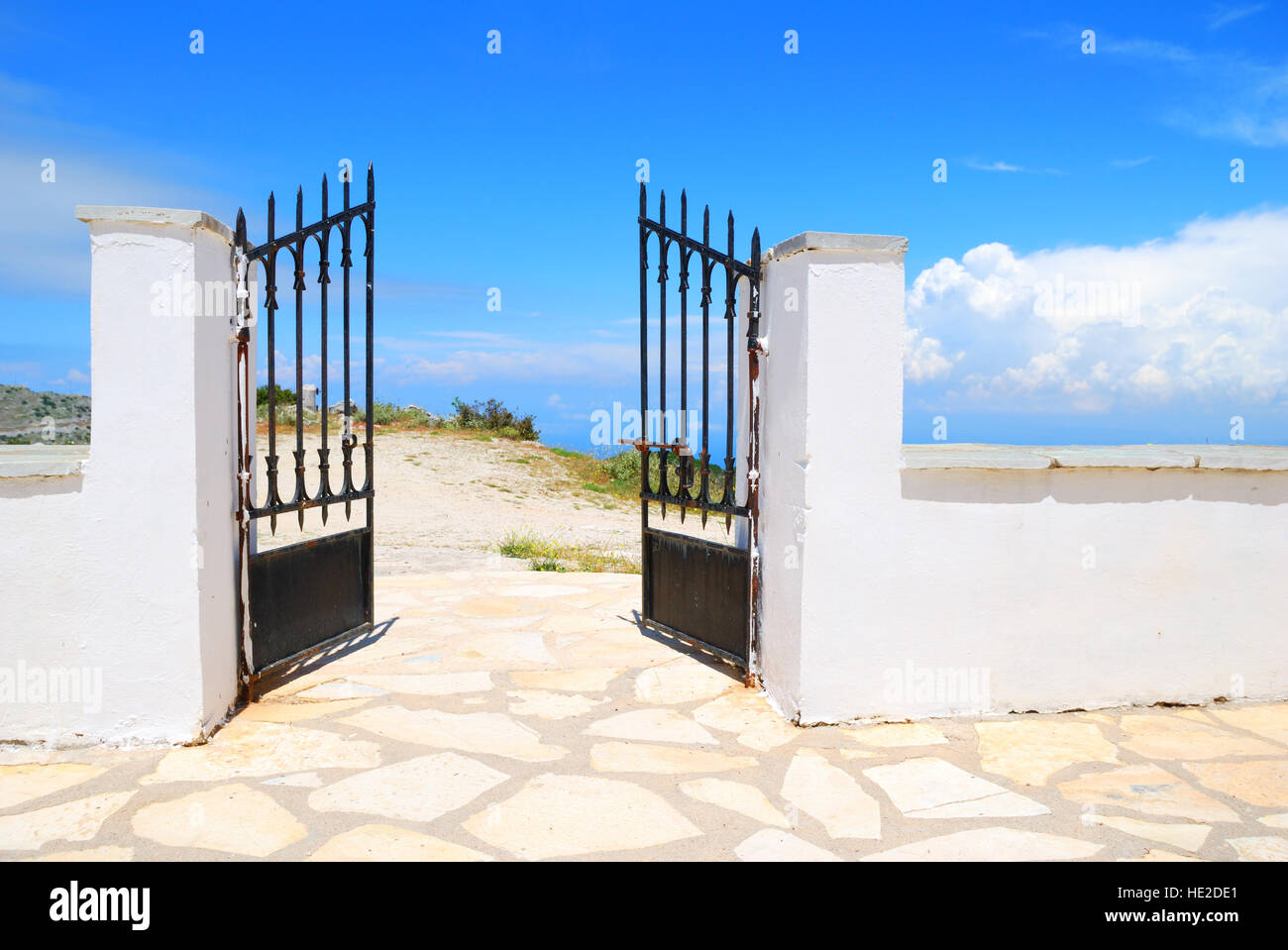 Opened iron gate in a white wall with blue sky behind Stock Photo - Alamy
