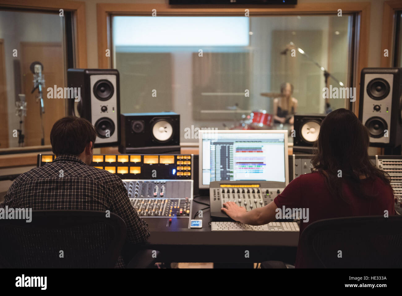 Rear view of audio engineers using sound mixer in recording studio ...