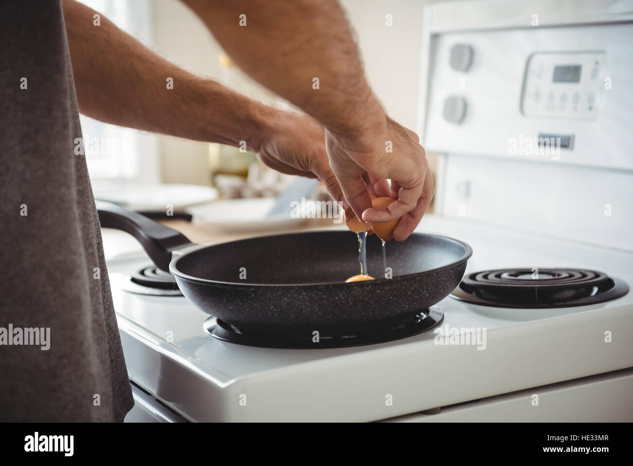 Mid section of man cracking an egg into a frying pan in the kitchen at ...