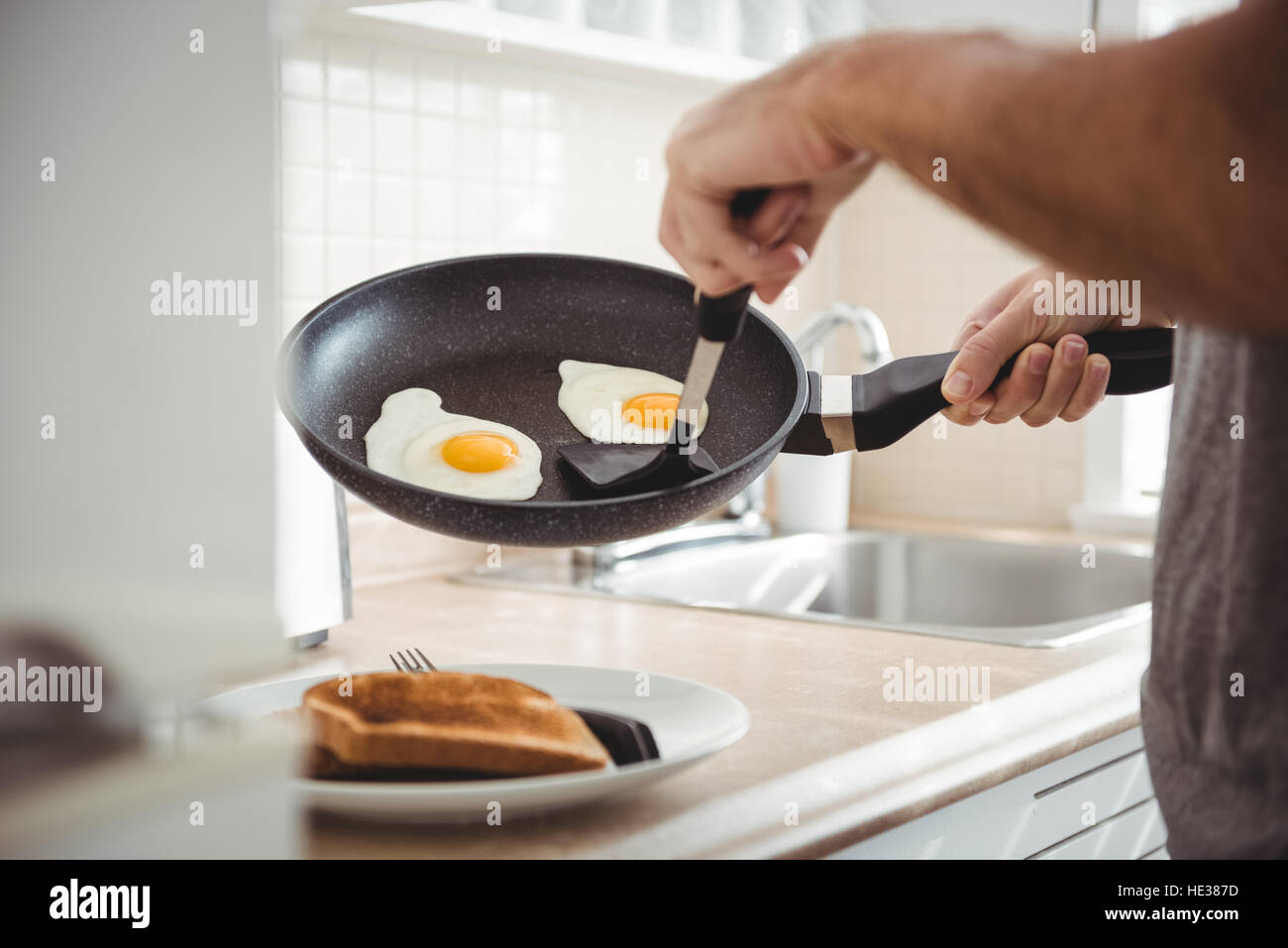 Mid section of man picking up fried eggs from cooking pan in kitchen at ...