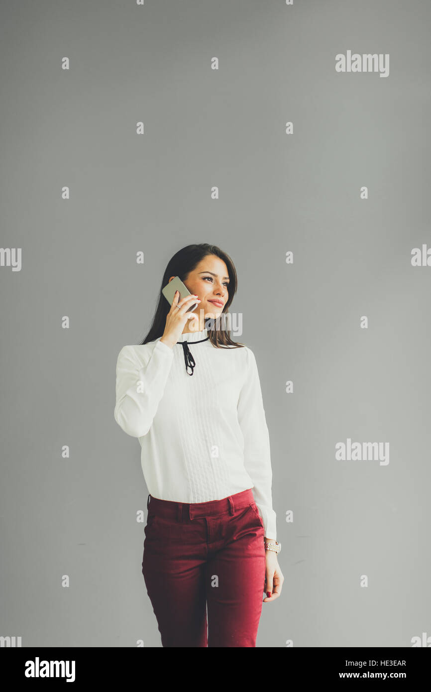 Pretty young woman with mobile phone by gray wall in the office Stock ...