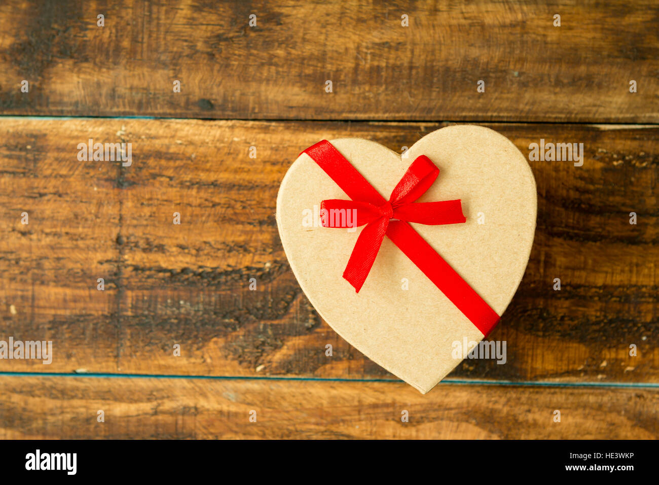 Beautiful gift with heart shape and red ribbon on a wooden background ...