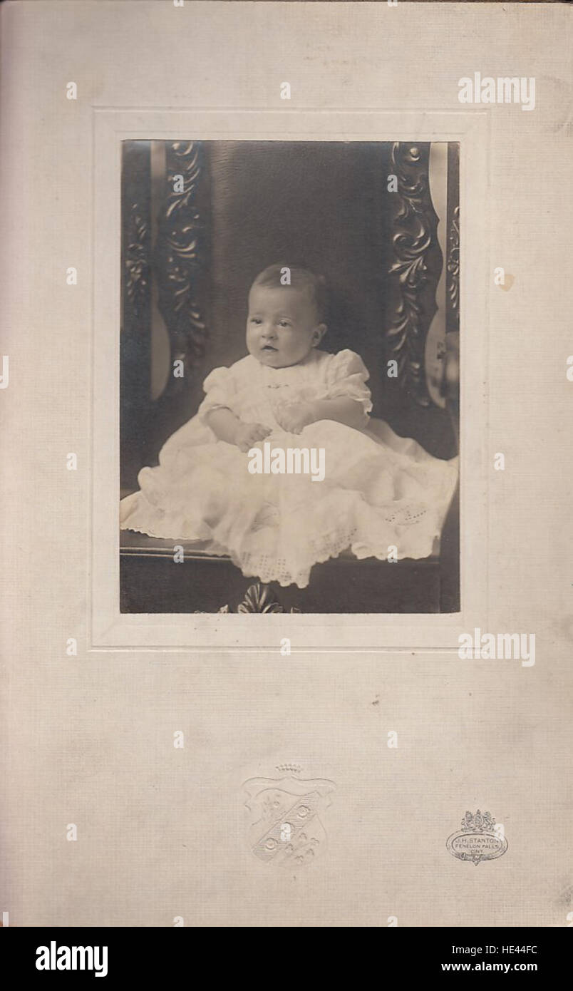 This historic photograph captures a baby sitting on a chair, offering a ...