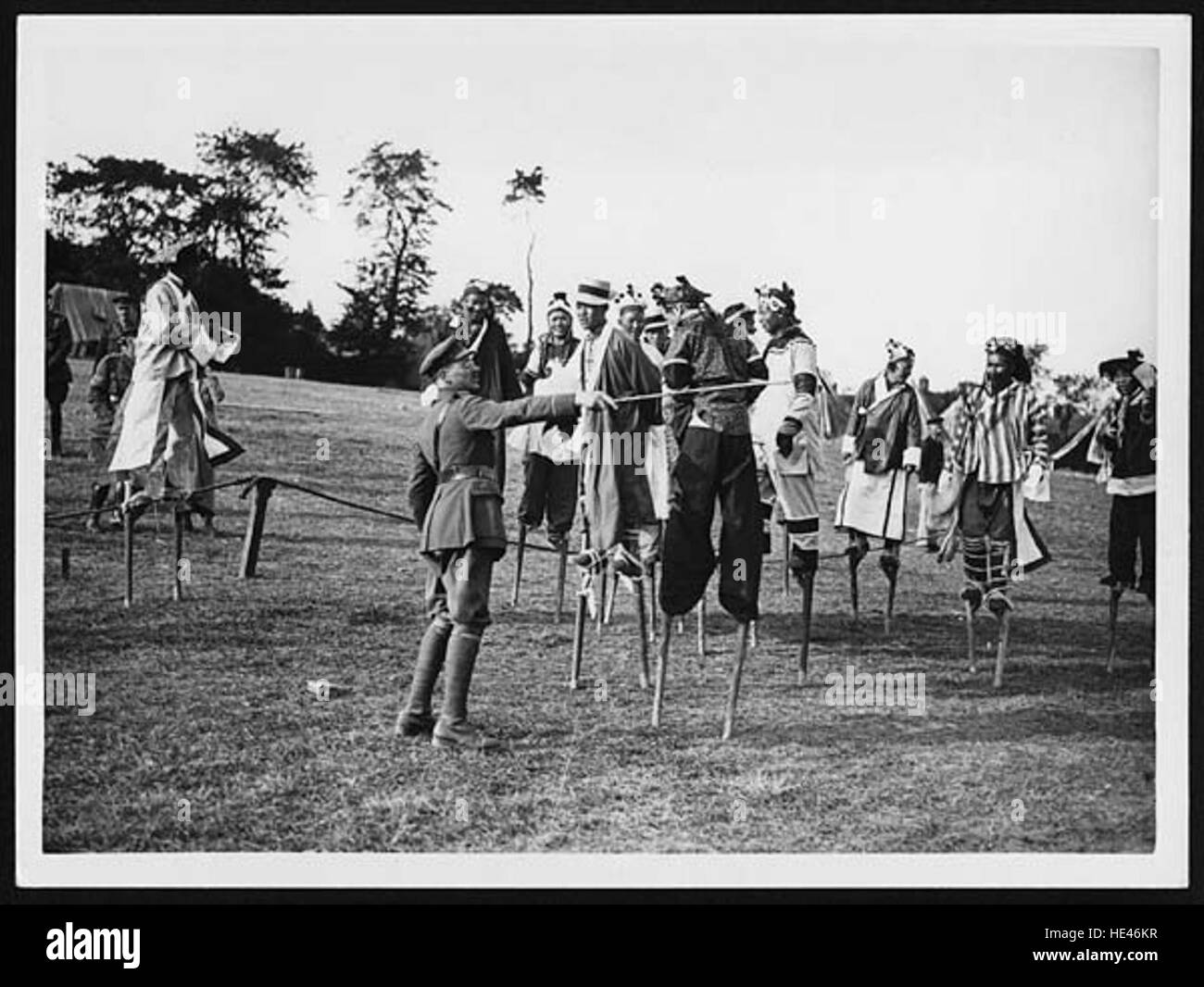 This historic image shows an officer directing a stilt walking party ...
