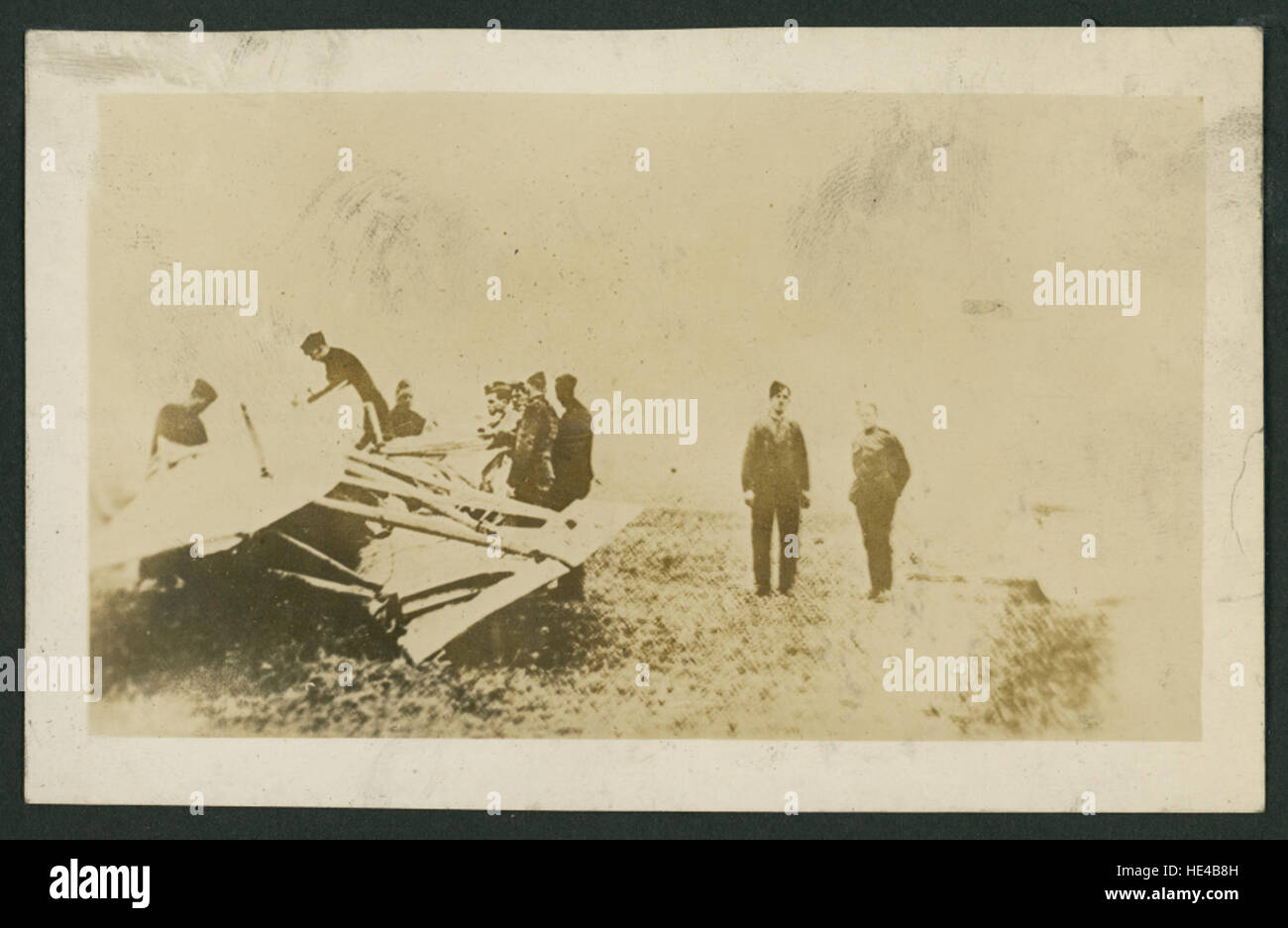 This historical image depicts soldiers alongside a crashed biplane ...