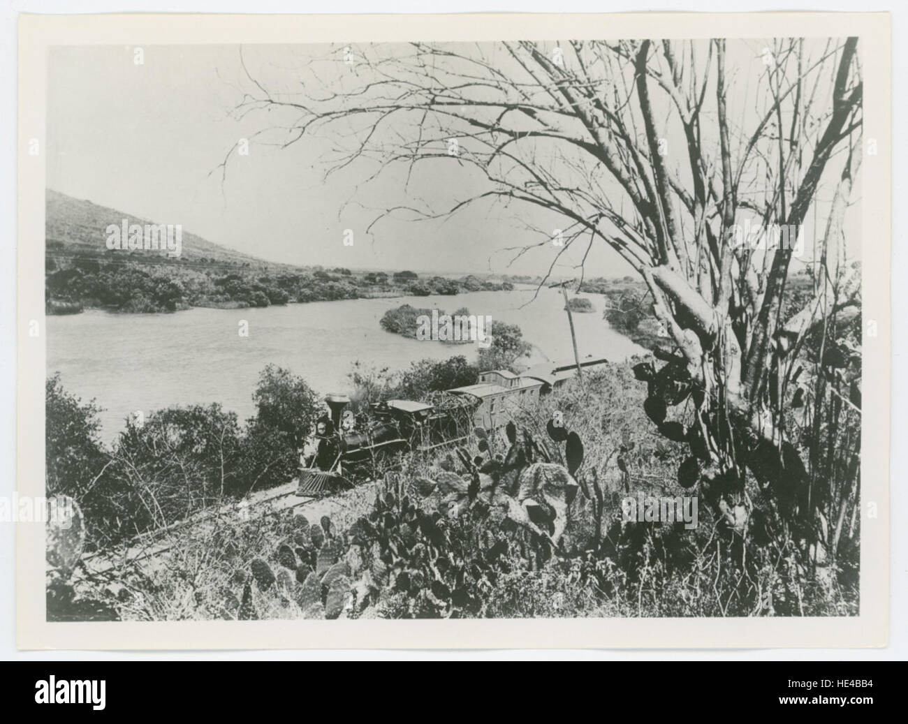 This historical image shows a train crossing over a river, emphasizing ...