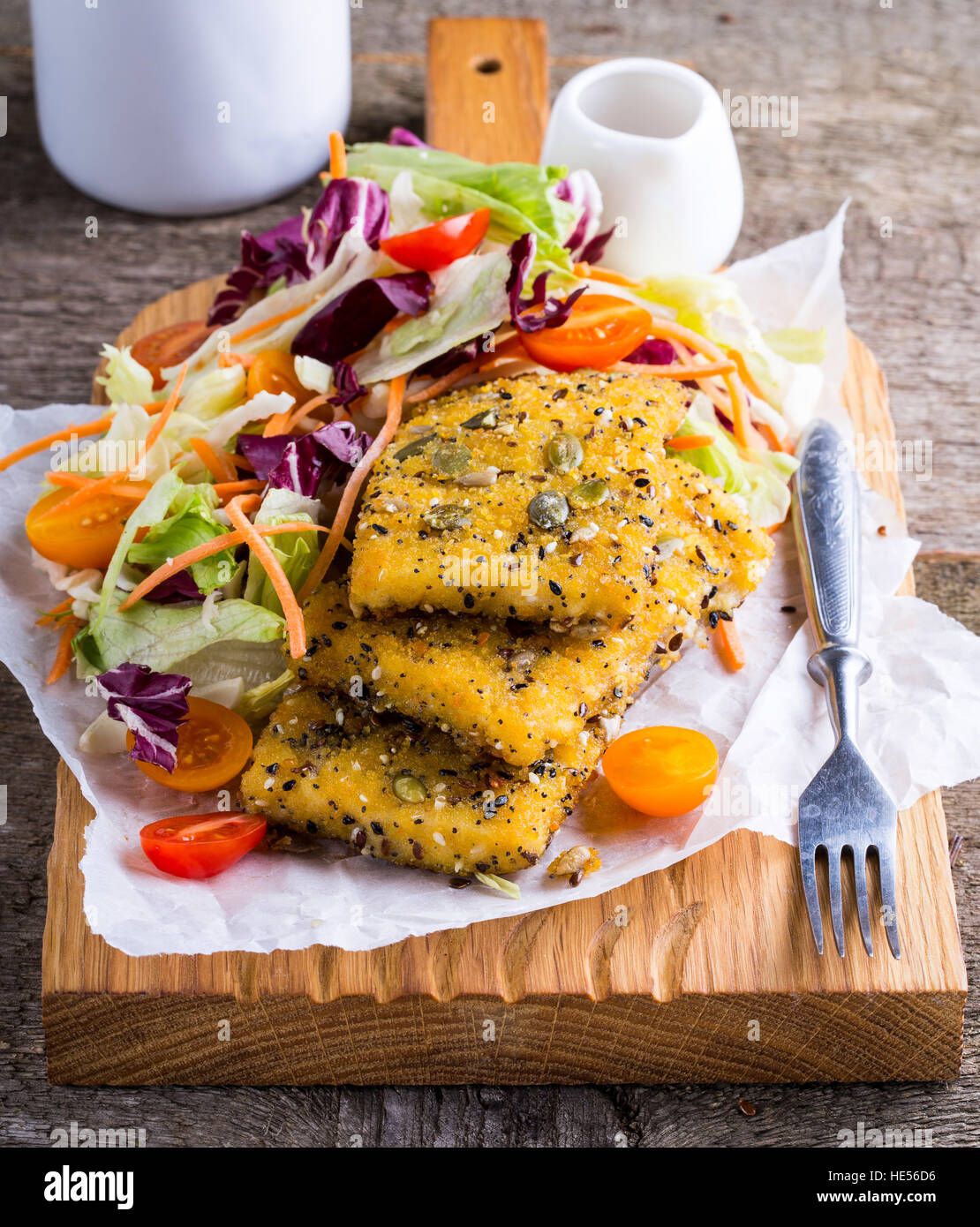 Coated fish fillet with fresh salad served on wooden board Stock Photo ...