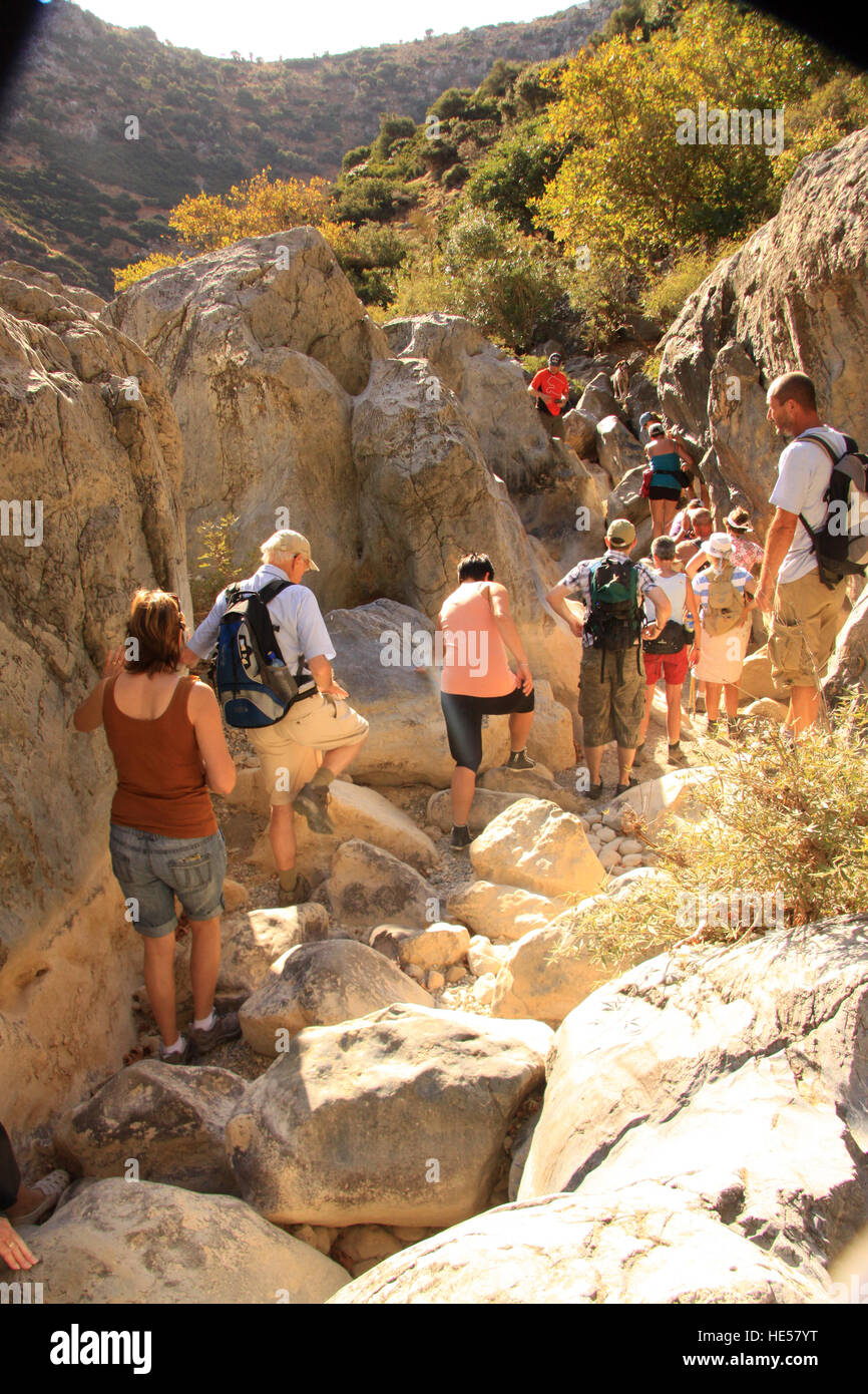 Tourists and holidaymakers on a guided walk along a dry river bed gorge ...