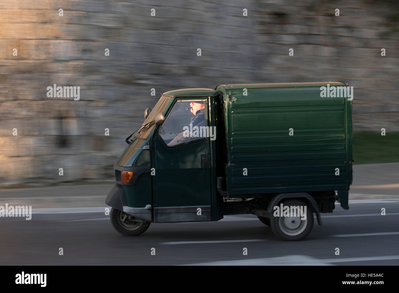 A driver smokes a cigar as he drives. Three wheeled Italian delivery ...