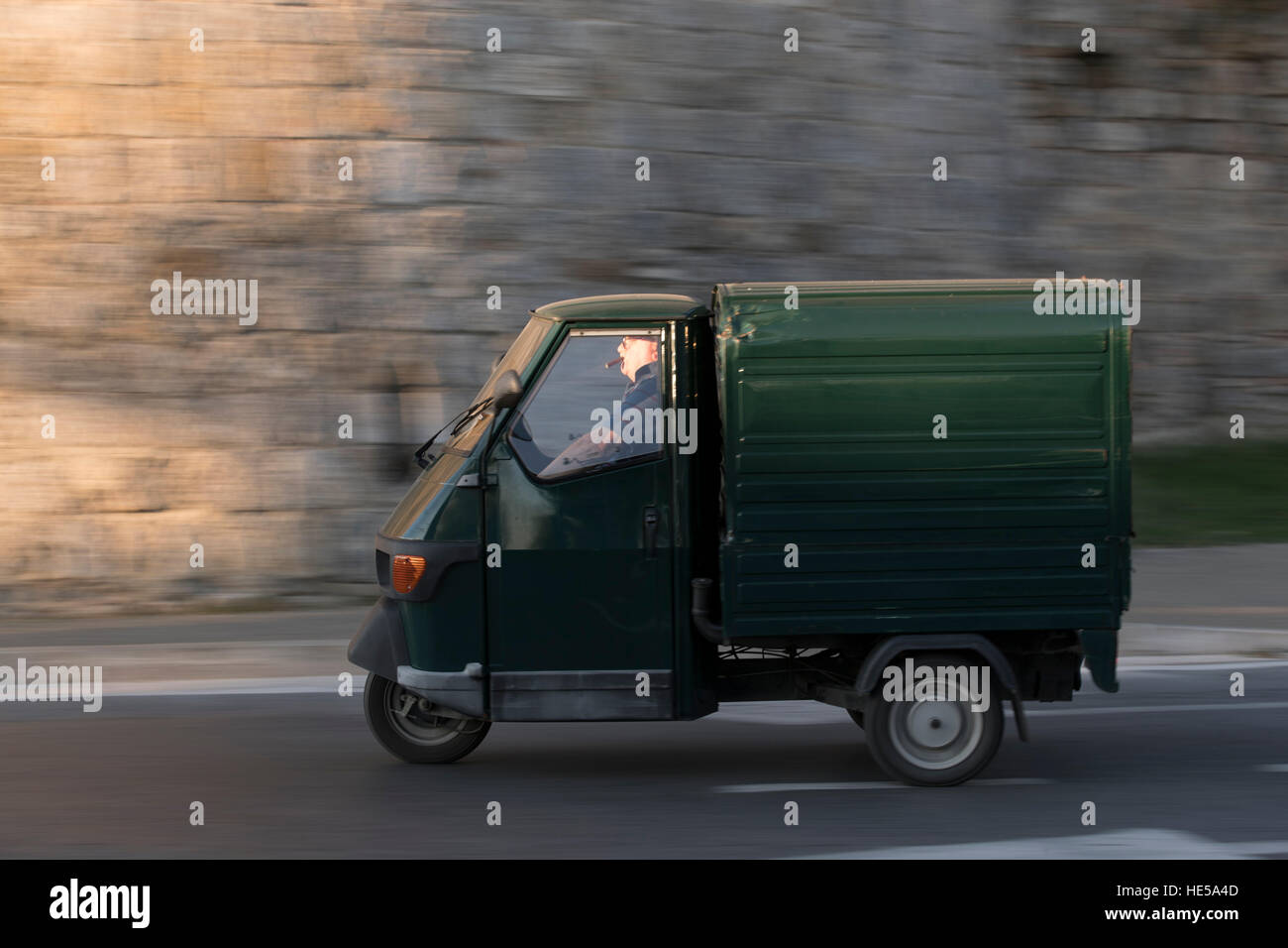 A driver smokes a cigar as he drives. Three wheeled Italian delivery ...