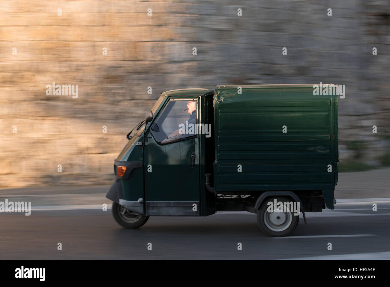 A driver smokes a cigar as he drives. Three wheeled Italian delivery ...