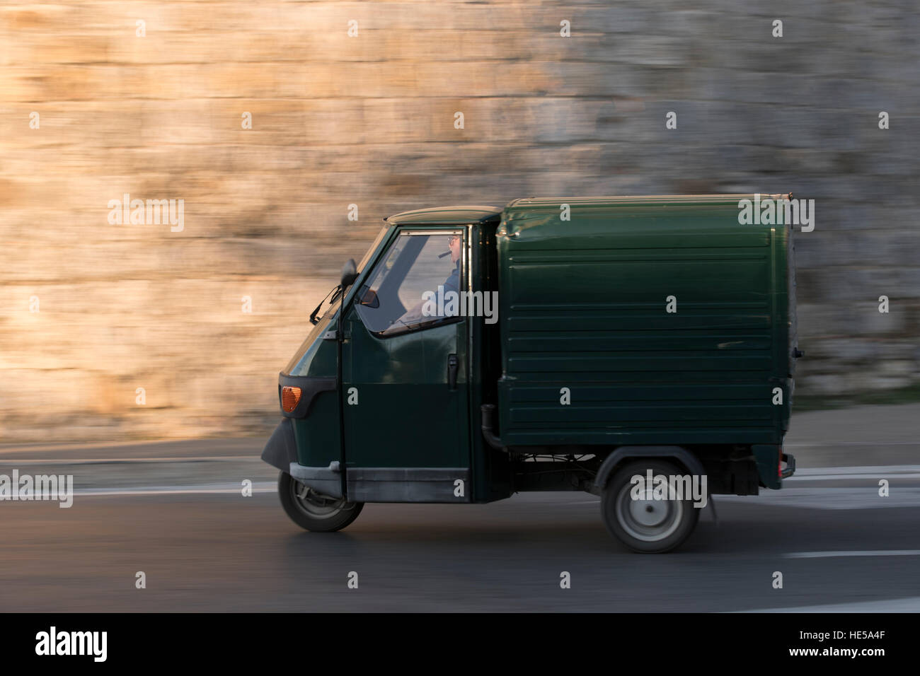 A driver smokes a cigar as he drives. Three wheeled Italian delivery ...