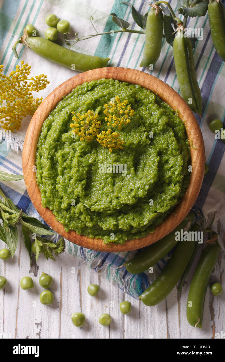 Puree of fresh green peas close up in a wooden bowl. Vertical top view ...
