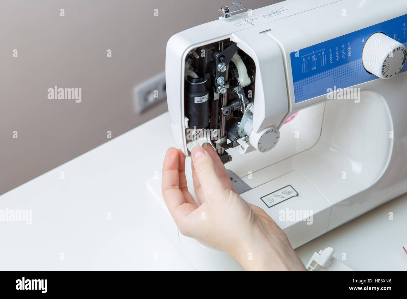 Young man repairing sewing machine standing on blank gray background ...