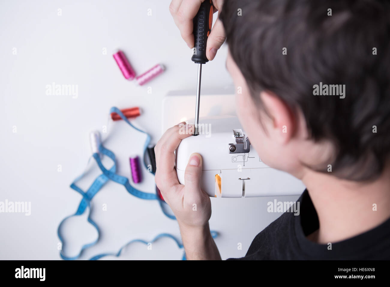 Man with screwdriver repairing sewing machine on empty gray background ...