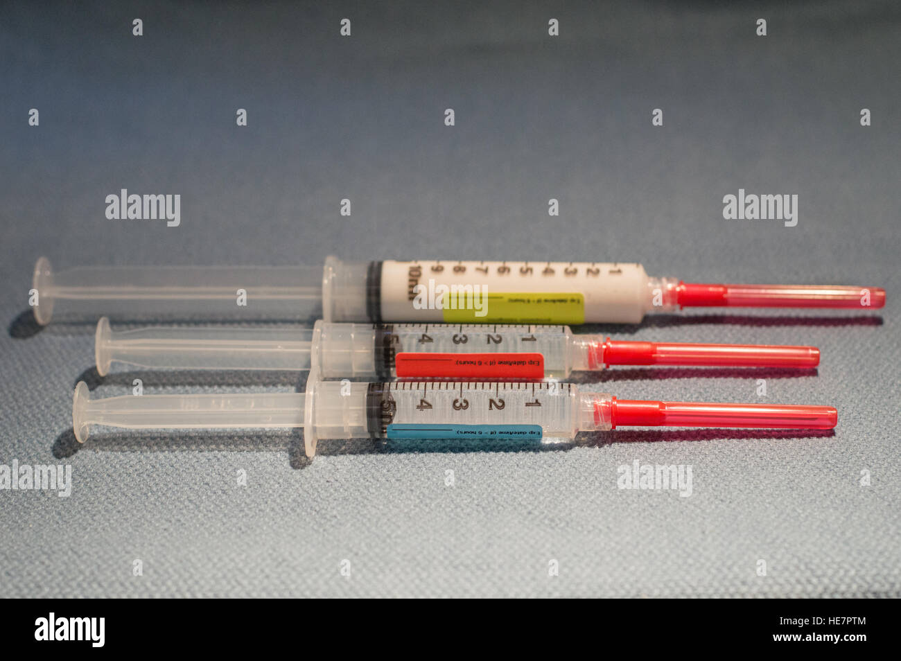 Three syringes with red capped needles containing labeled generic ...